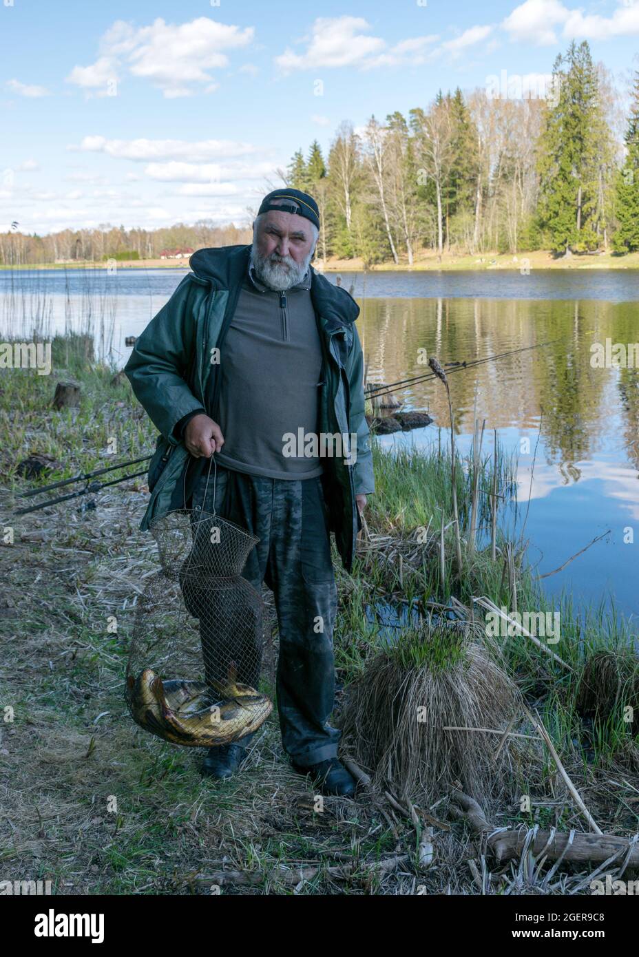 spring landscape with a lake, a fisherman shows the caught fish on the ...