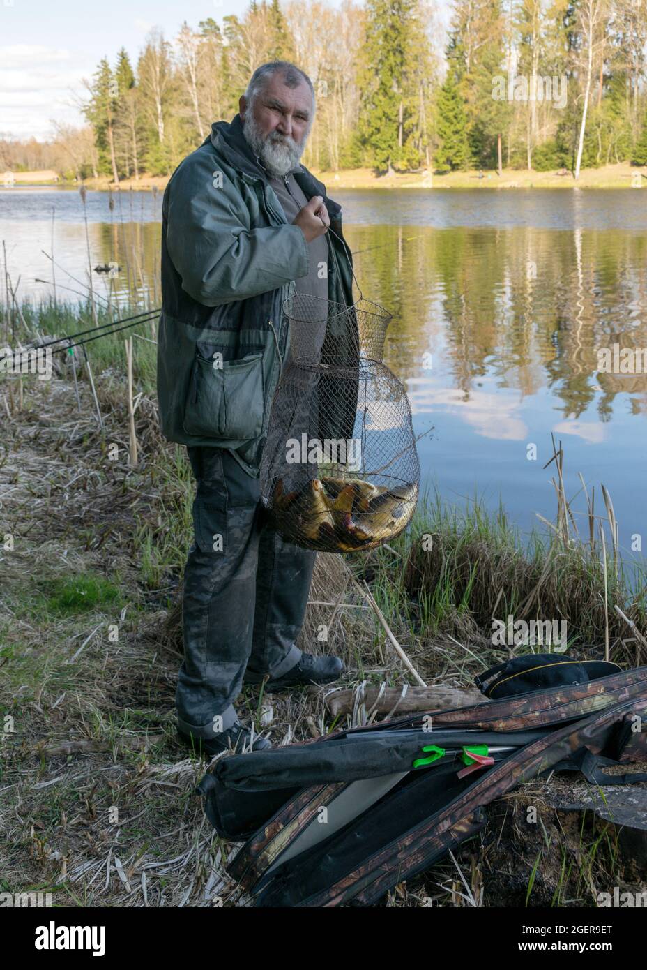 spring landscape with a lake, a fisherman shows the caught fish on the ...