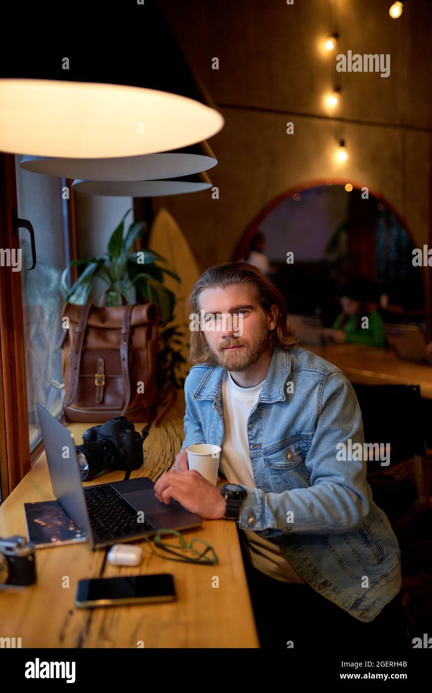 Hipster man sitting at cafeteria table with modern laptop, freelancer ...