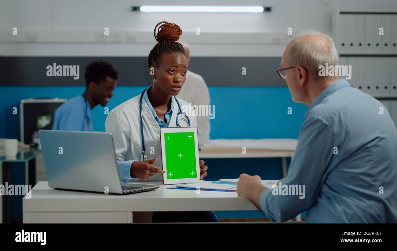 Young doctor with green screen technology on tablet explaining chroma ...