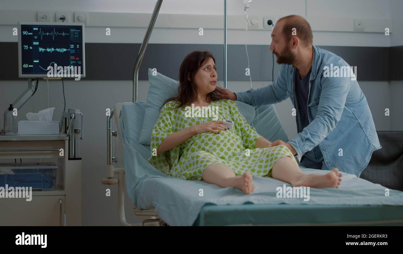 Young woman going into labor in hospital ward sitting with husband ...