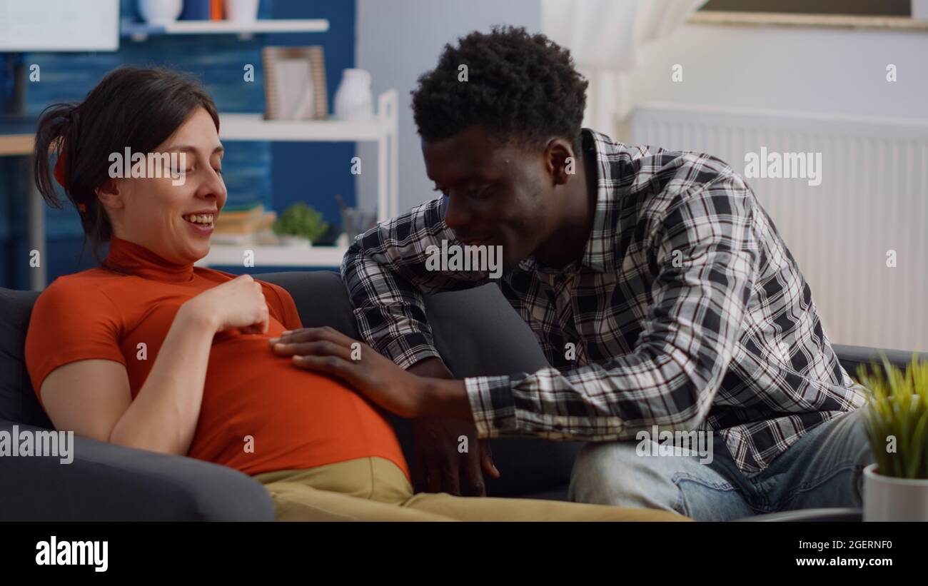 Pregnant interracial couple sitting on living room couch. African ...
