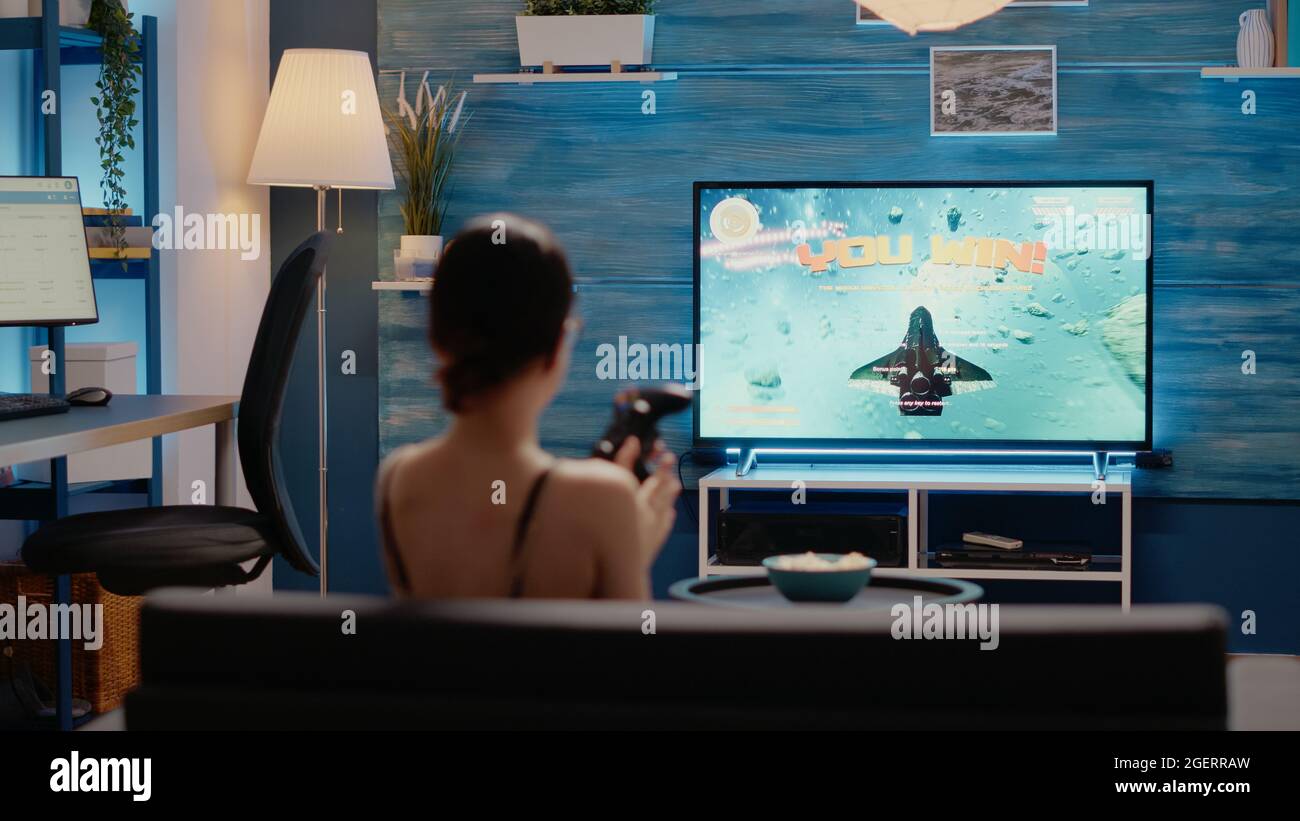 Young woman holding wireless joystick in living room with technology at ...