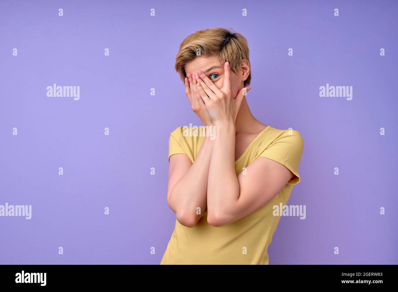 Scared short-haired female looking at camera through one eye, closing ...