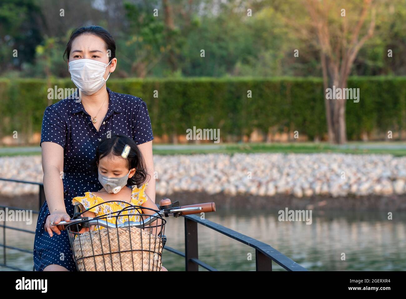 Mother and daughter wearing protective face masks riding a bike in a ...