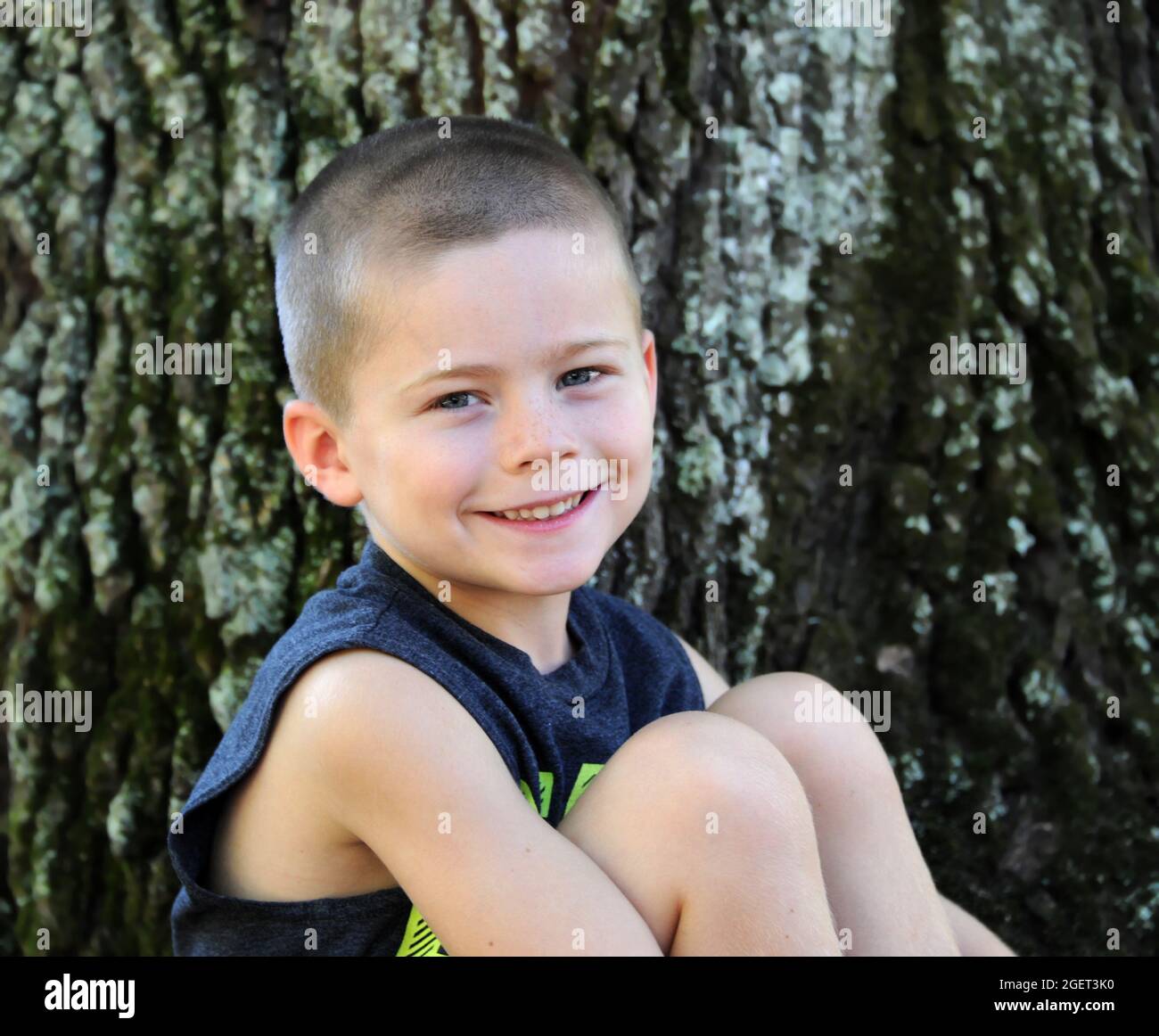 Boyish grin spreads across this little boys face. He is sitting outside ...