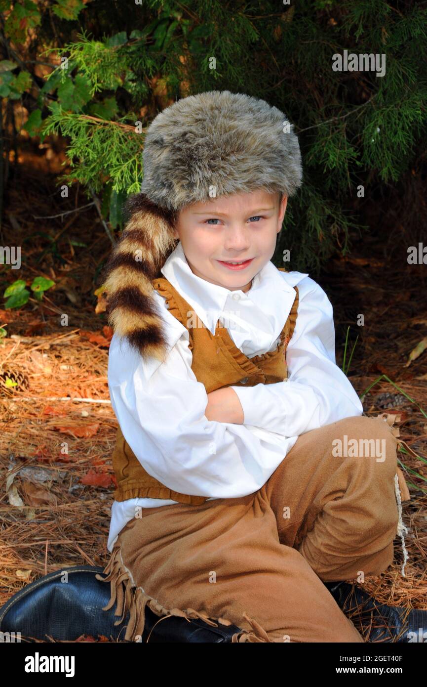Little boy, wearing a coon skinned cap and fringed buckskins, kneels in ...