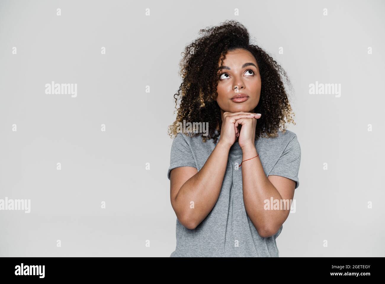 A pensive woman looking-up with hands propping her chin while standing ...