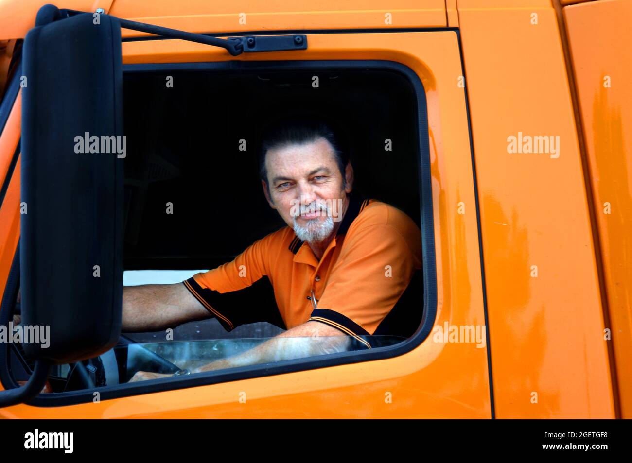 Attractive man leans on the cab of the eighteen wheeler he is driving ...