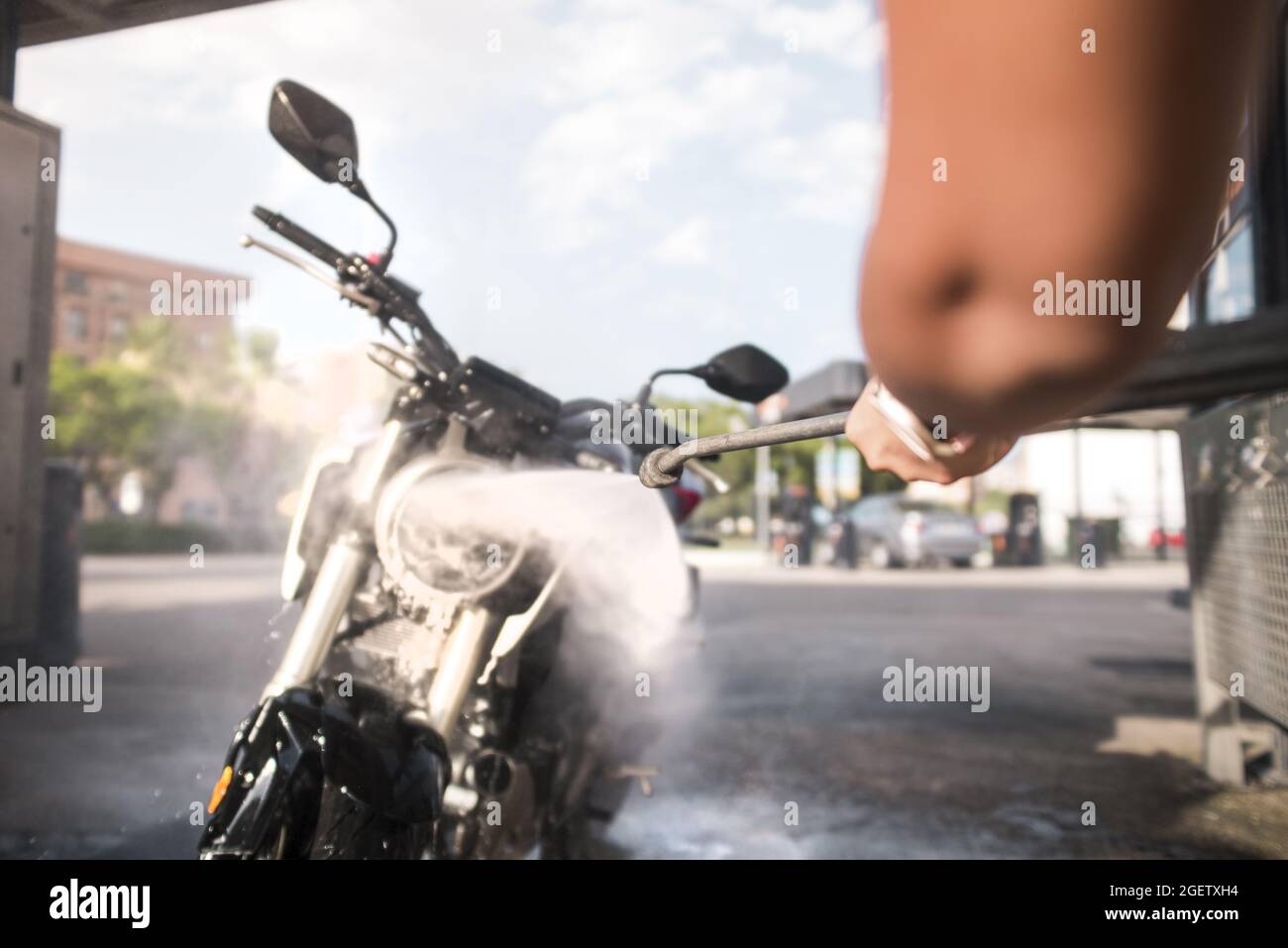 Closeup of a person washing a motorcycle with a water spray gun ...