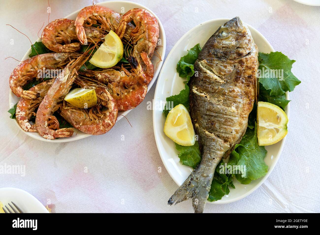 Grilled sea fish and prawns on a white plate with lettuce and lemon ...