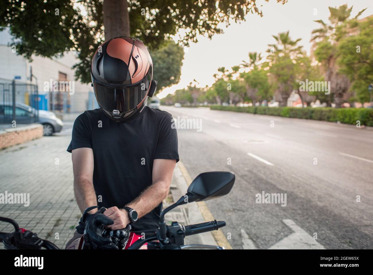 Young biker with a helmet on putting on the gloves for driving a ...