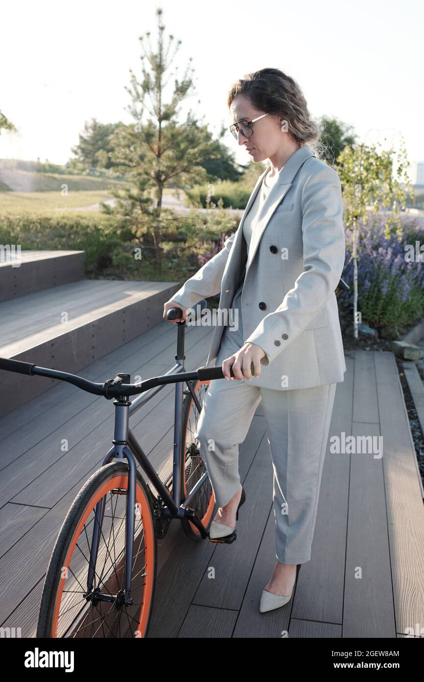 Young attractive businesswoman getting on bicycle on staircase in urban ...