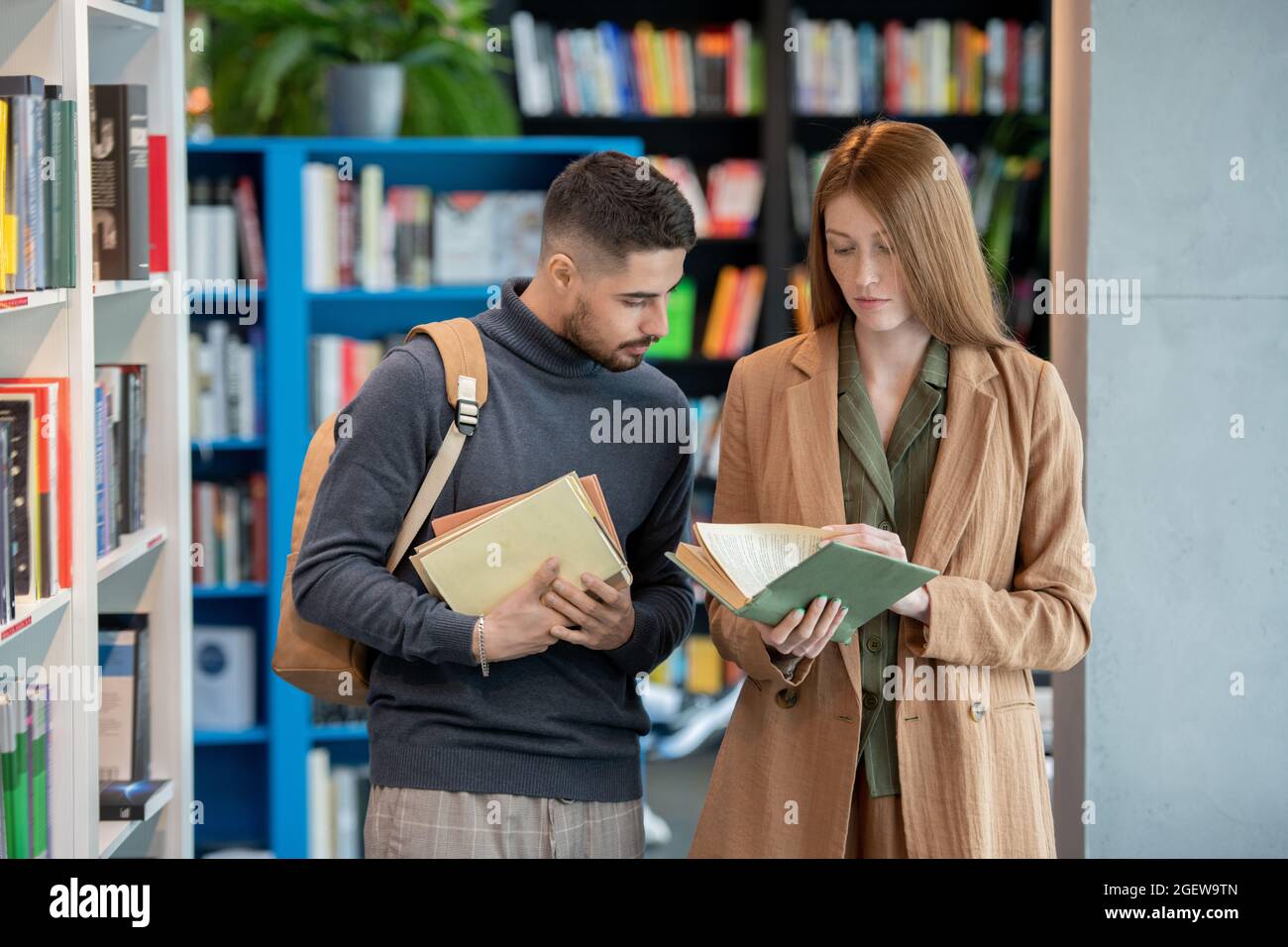 Two young students choosing books in college library or large bookshop ...