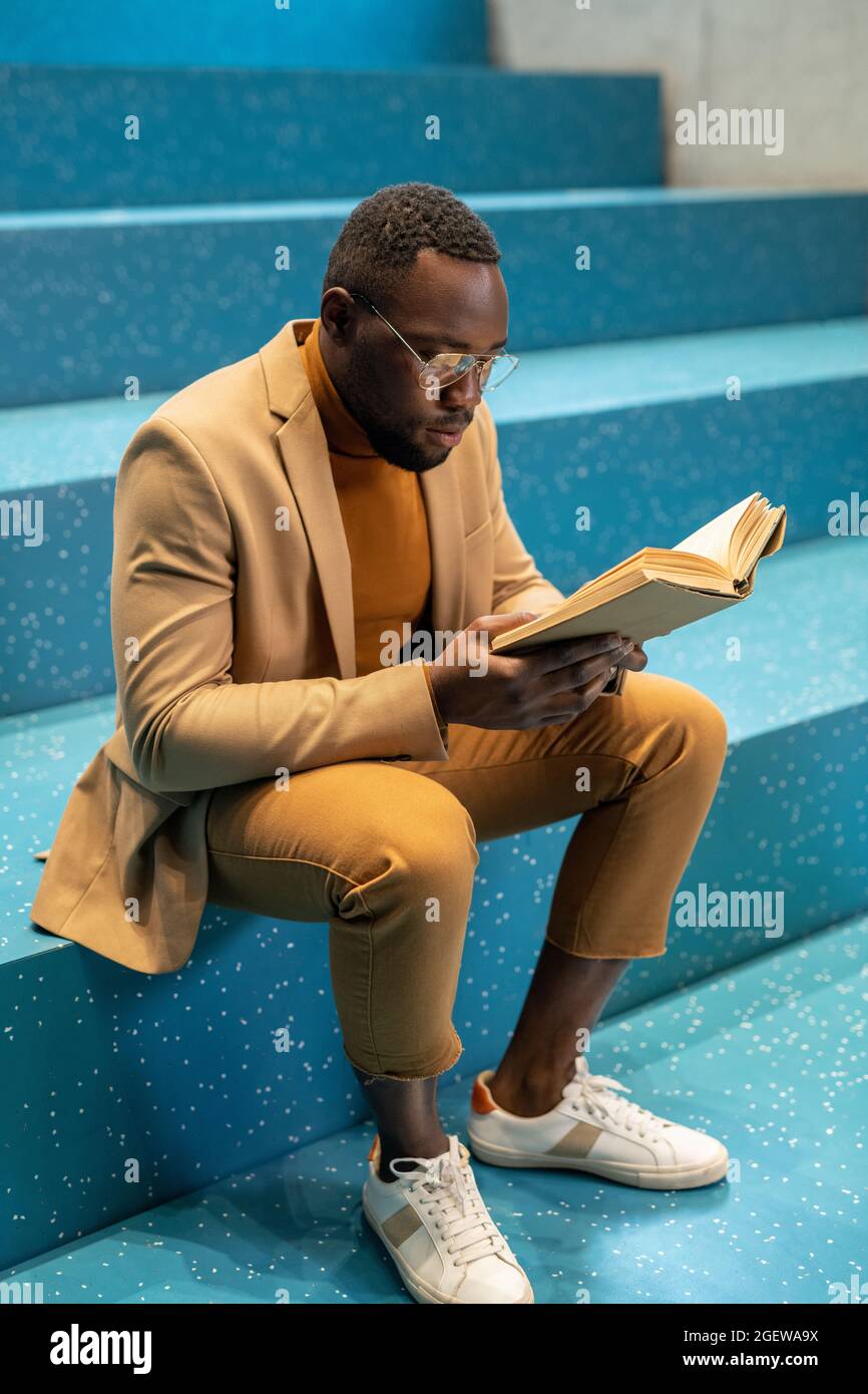 Contemporary African student reading book on blue staircase after ...