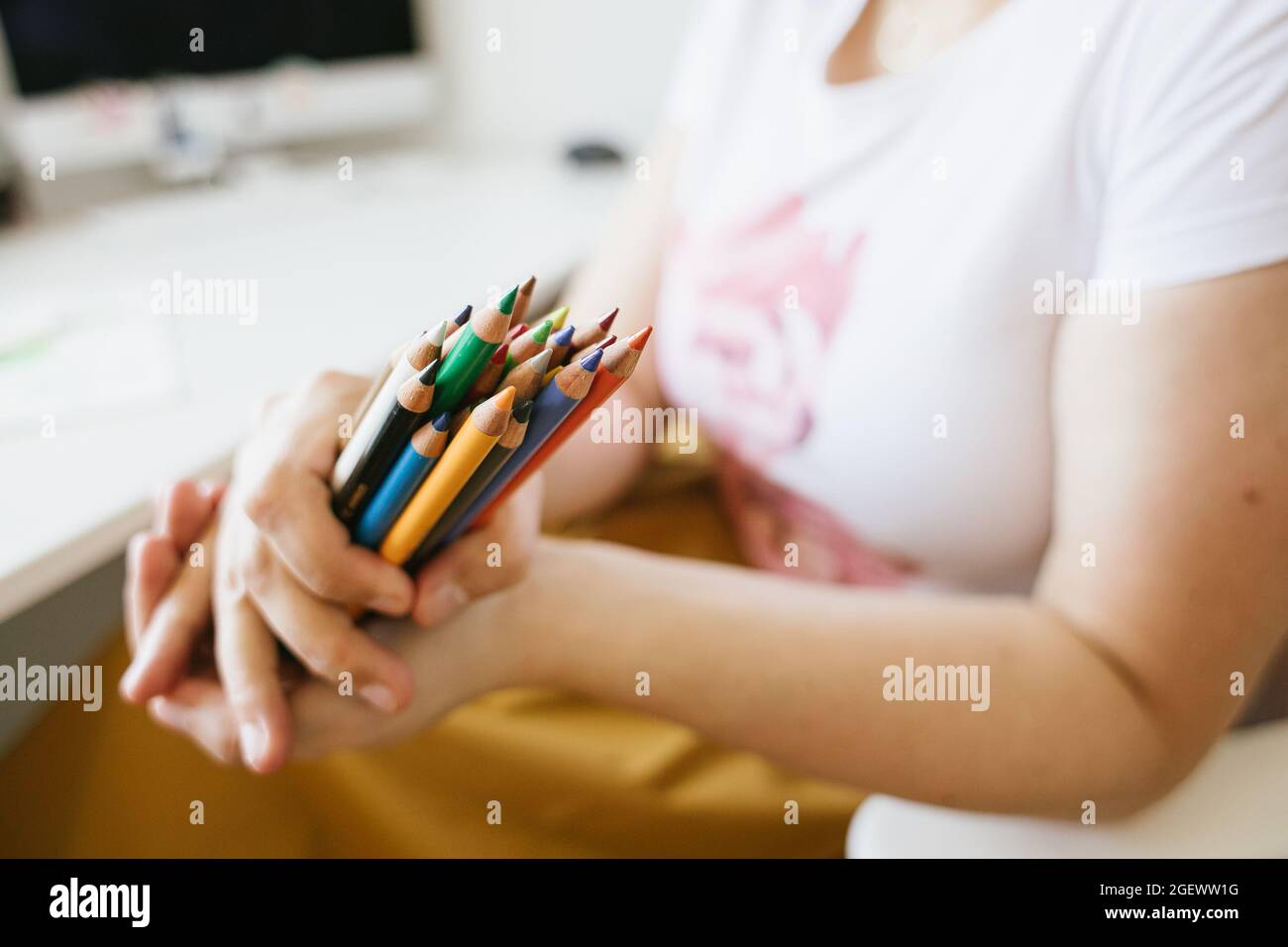 a bunch of colour pencils in woman's hands , computer desk in ...