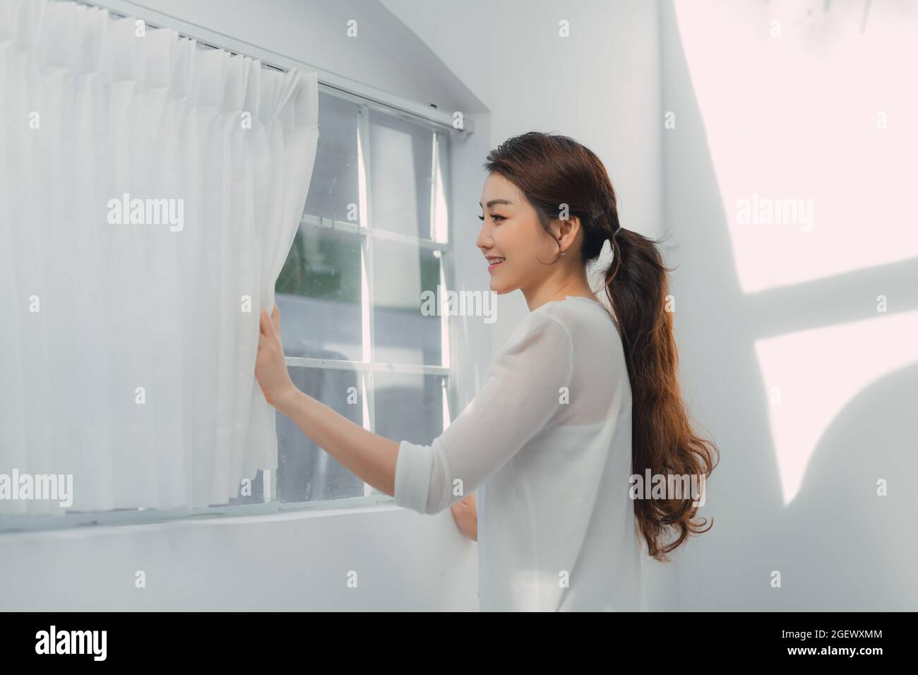 young woman standing in front of the bedroom window looking outside ...