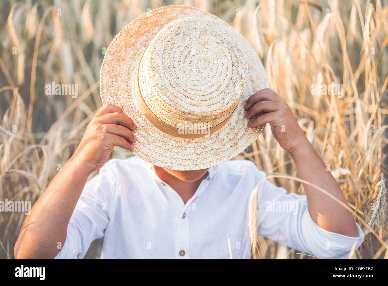 Faceless. cute kid boy covers his face straw hat on wheat field. A ...
