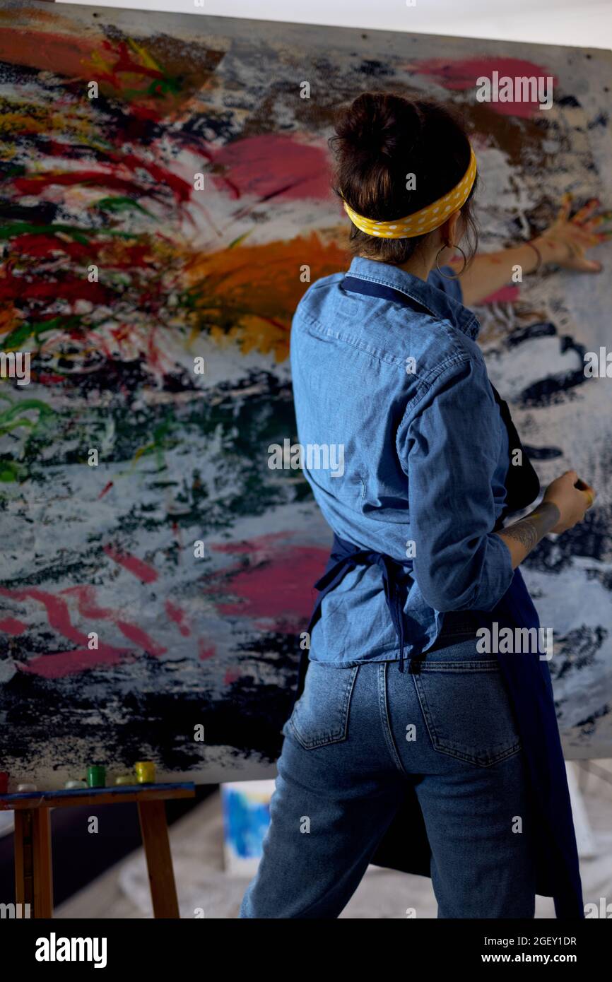 Back view of young female painter creating a large modern abstract oil ...