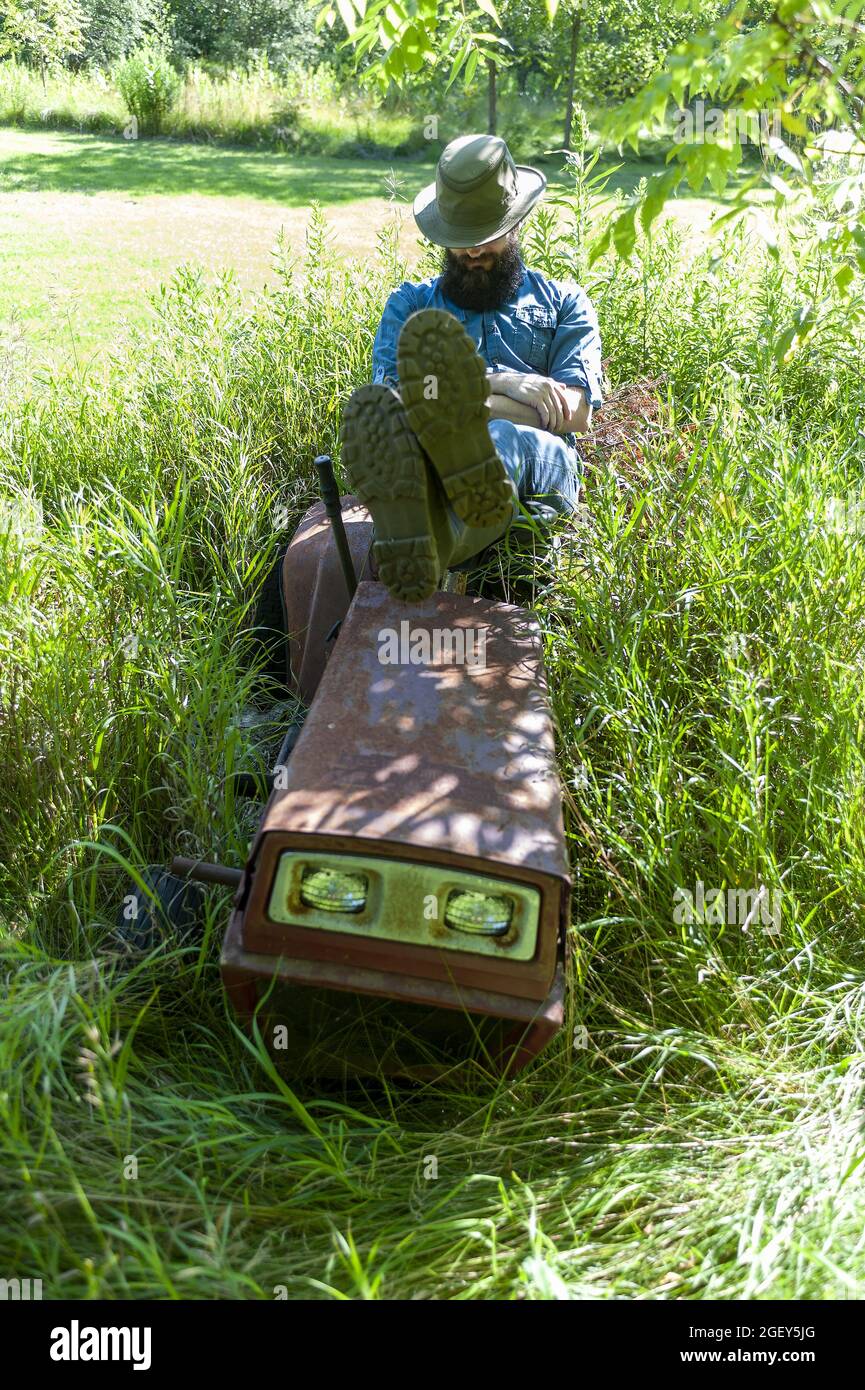 A handsome Caucasian rancher sitting on an old grass cutter in the ...