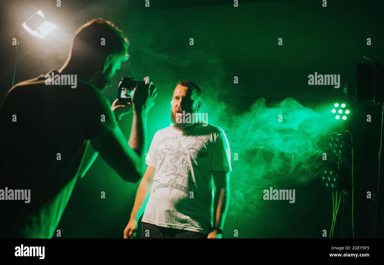 A cameraman filming a Caucasian man for a music video in green lights ...
