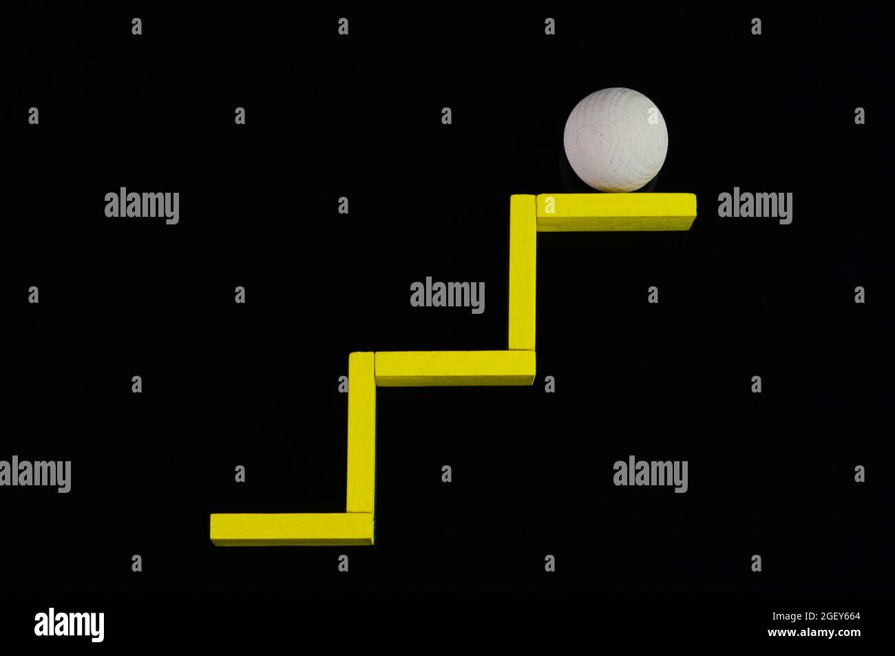 Wooden ball climbing on top of yellow steps Stock Photo - Alamy