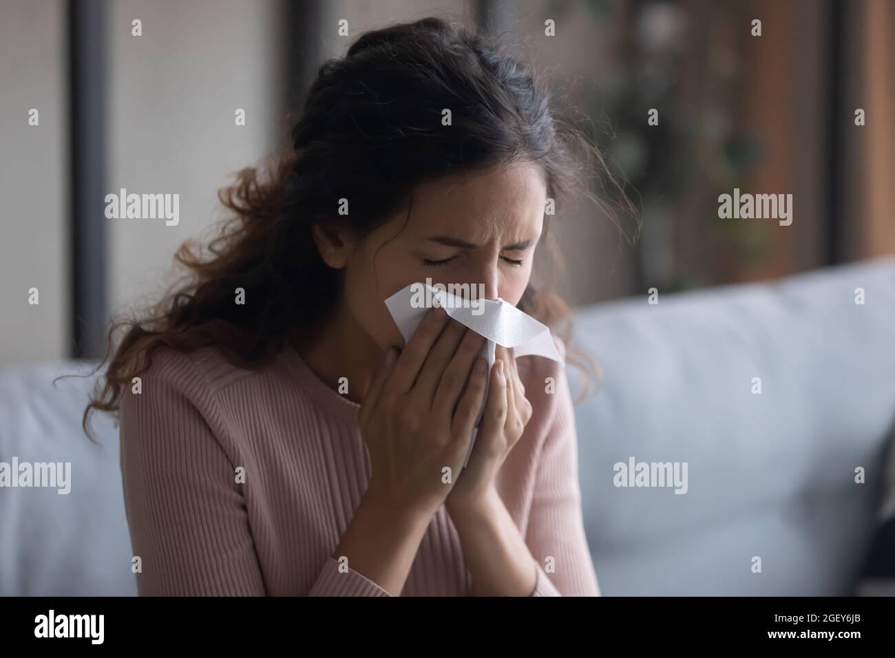 Sick young woman sitting indoors holding tissue blowing running nose ...