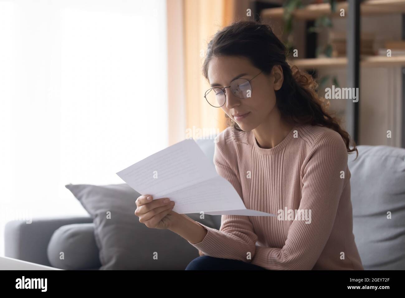 Serious woman wear glasses reading letter seated on sofa indoor Stock ...