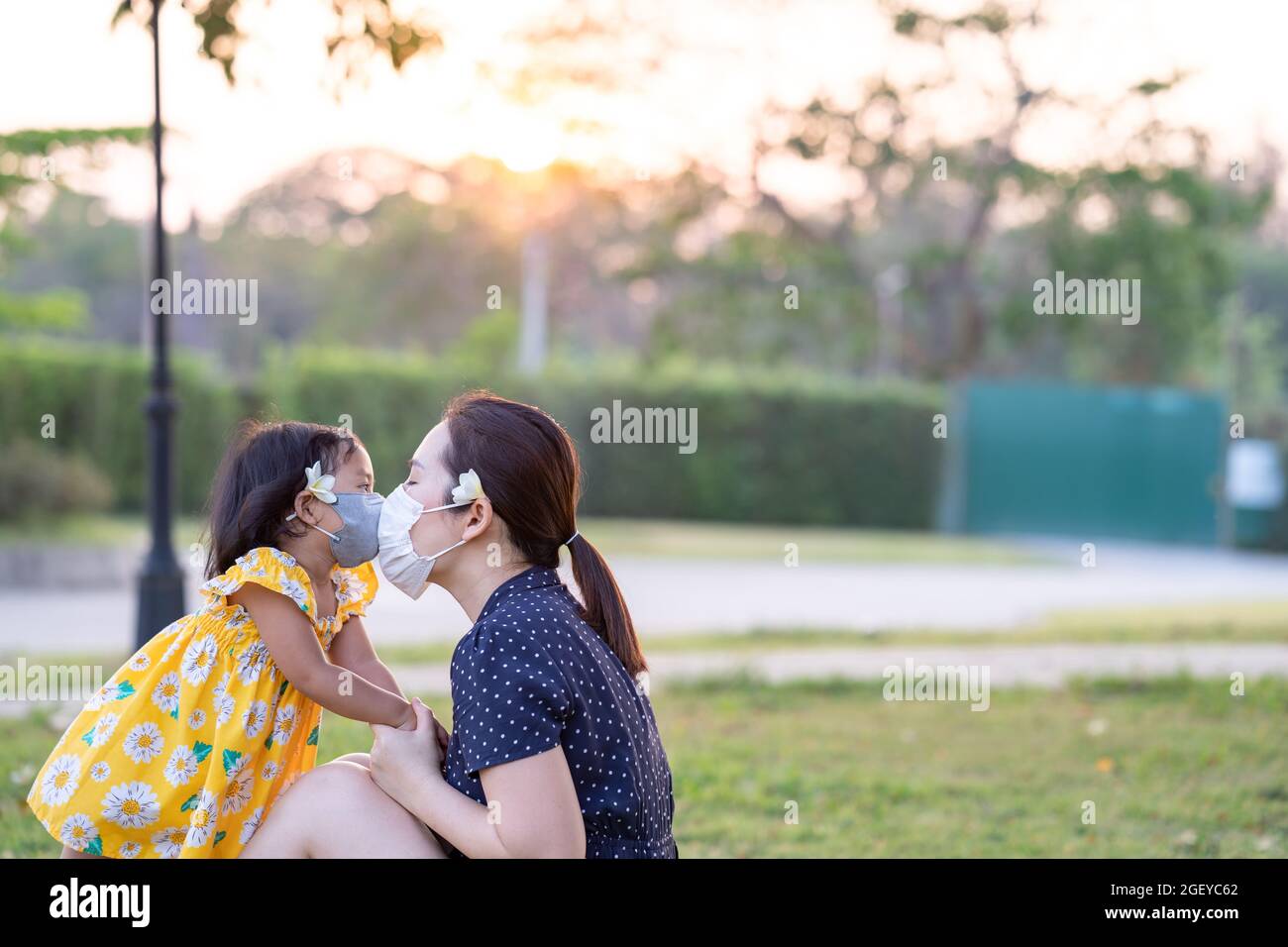 A mother and daughter sitting at the park wearing a medical face mask ...