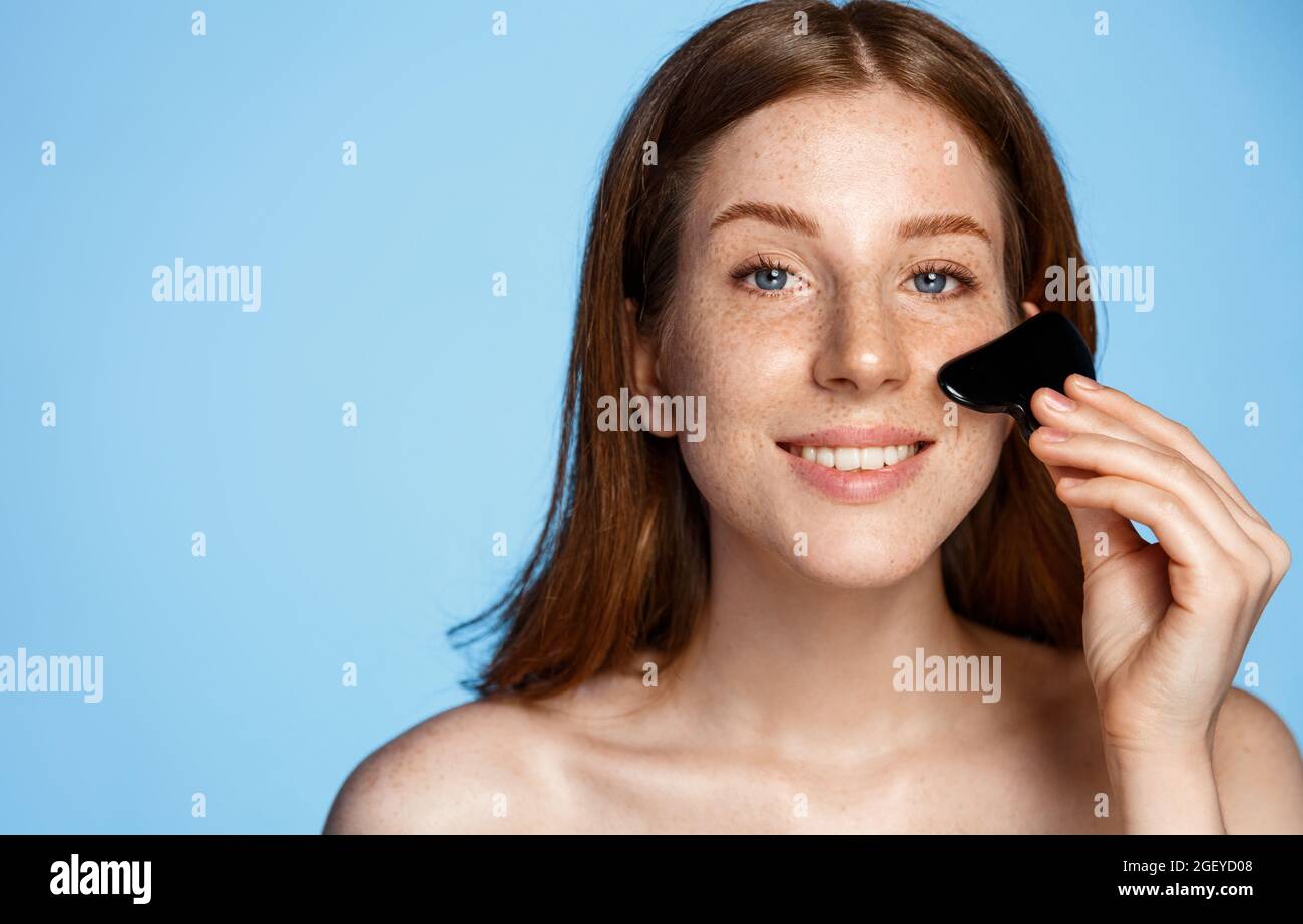 Smiling teen girl holds black gua sha scrapper near face, guasha facial ...
