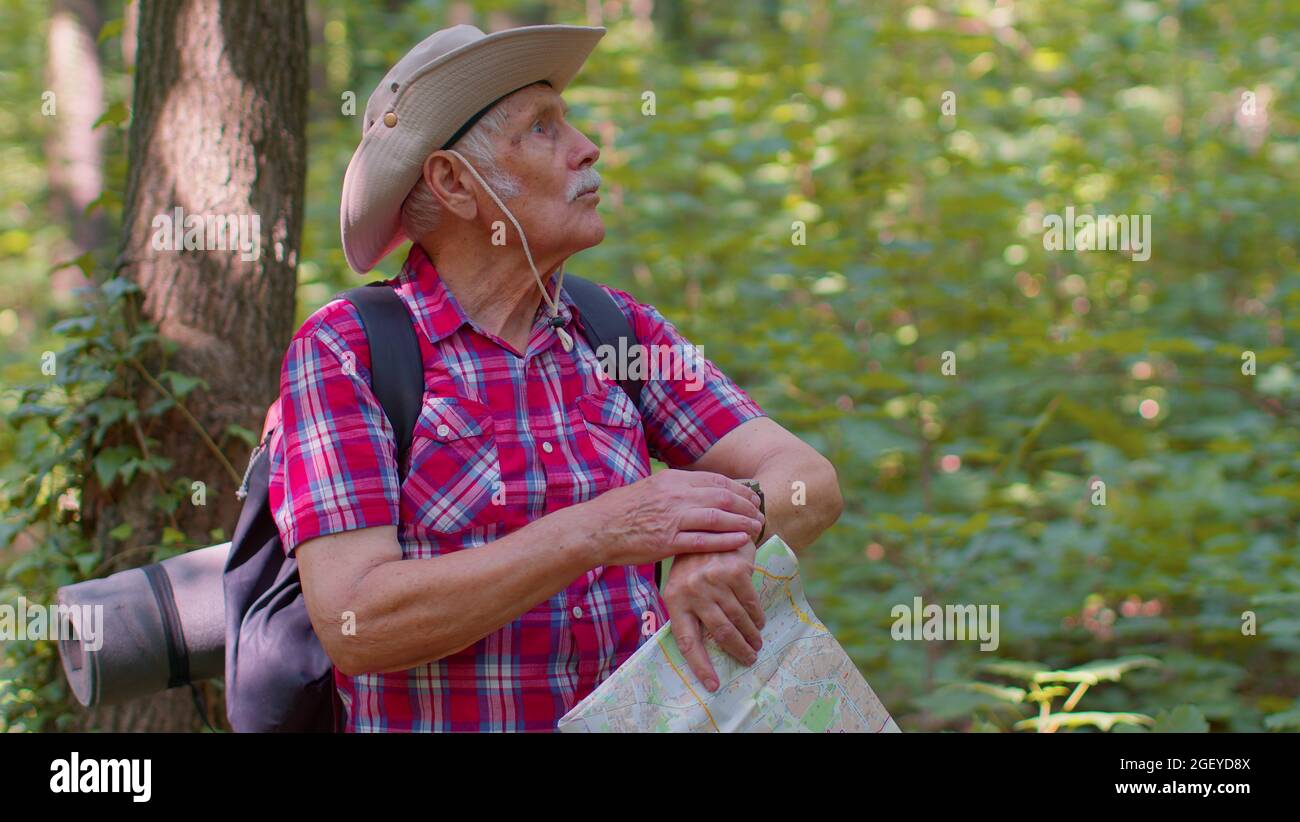 Senior old tourist grandfather man lost and looking at map and compass ...