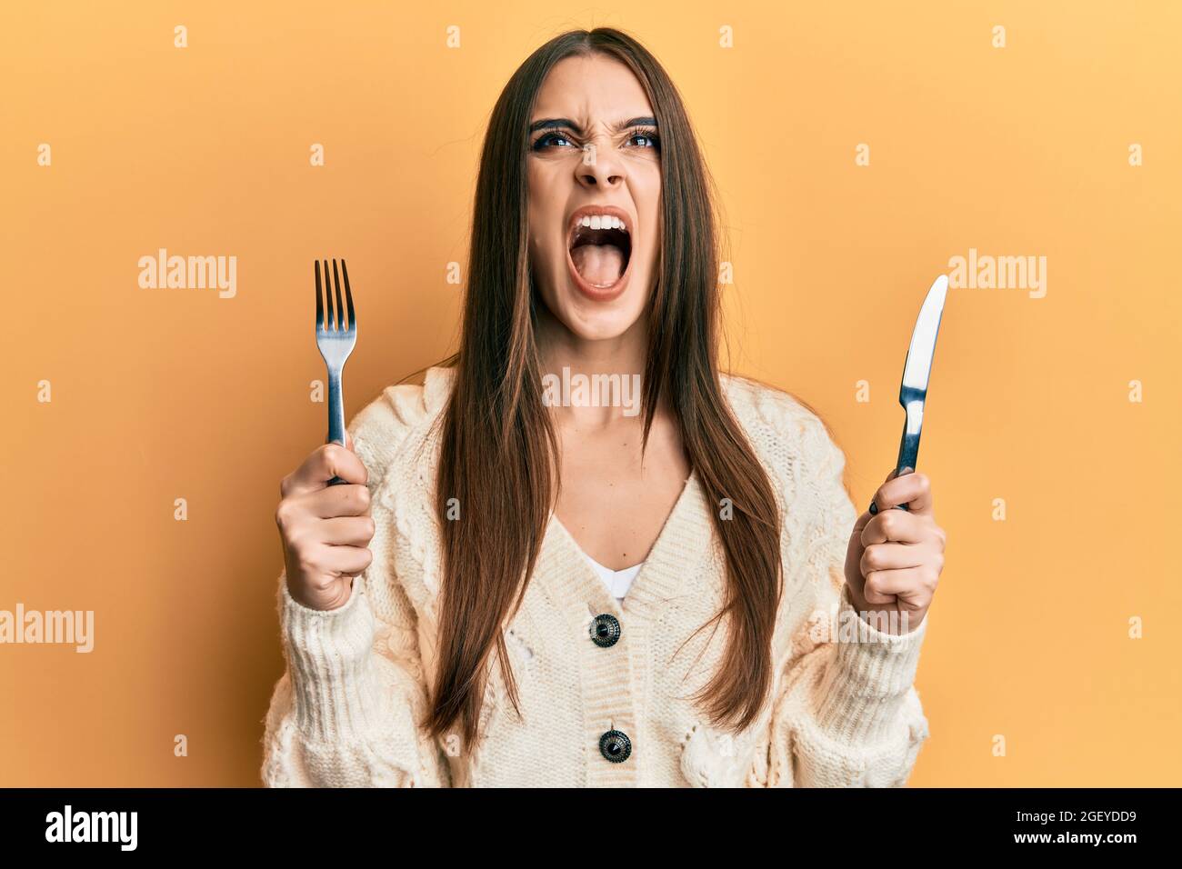 Beautiful brunette young woman holding fork and knife ready to eat ...