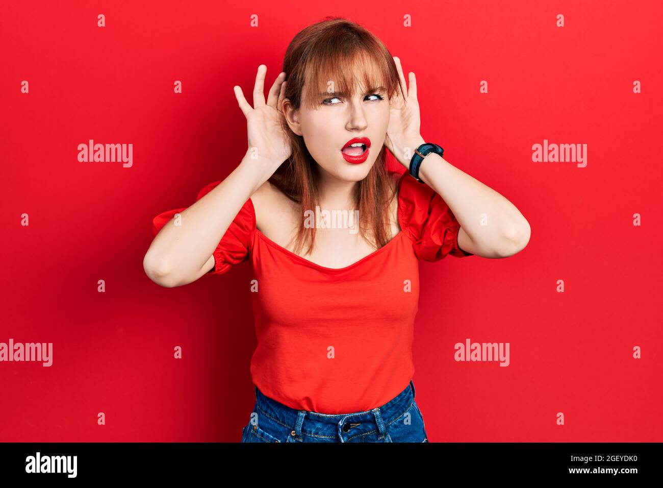 Redhead young woman wearing casual red t shirt trying to hear both ...