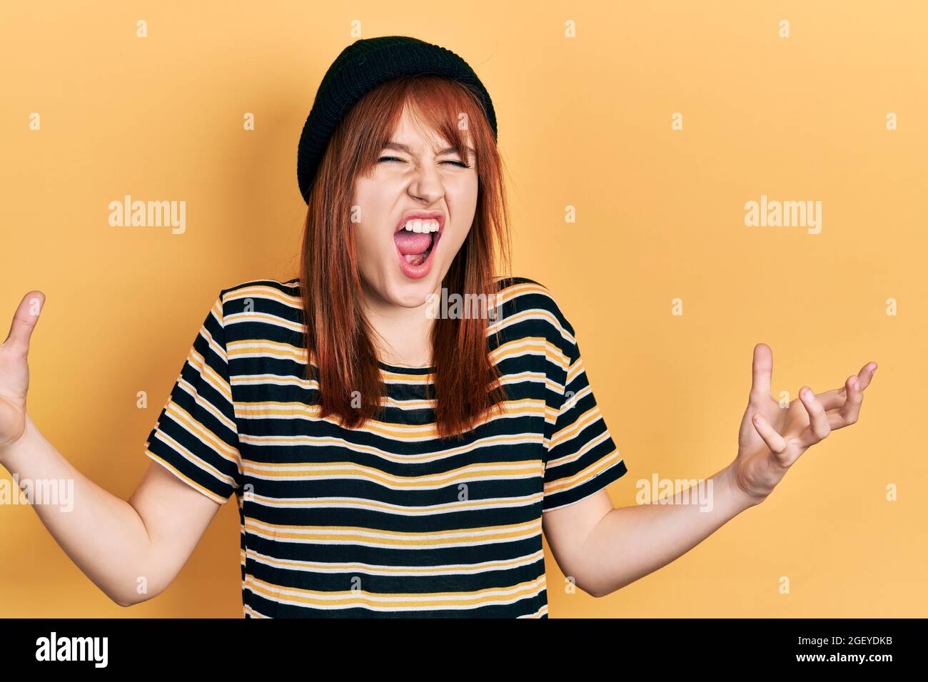 Redhead young woman wearing wool cap crazy and mad shouting and yelling ...