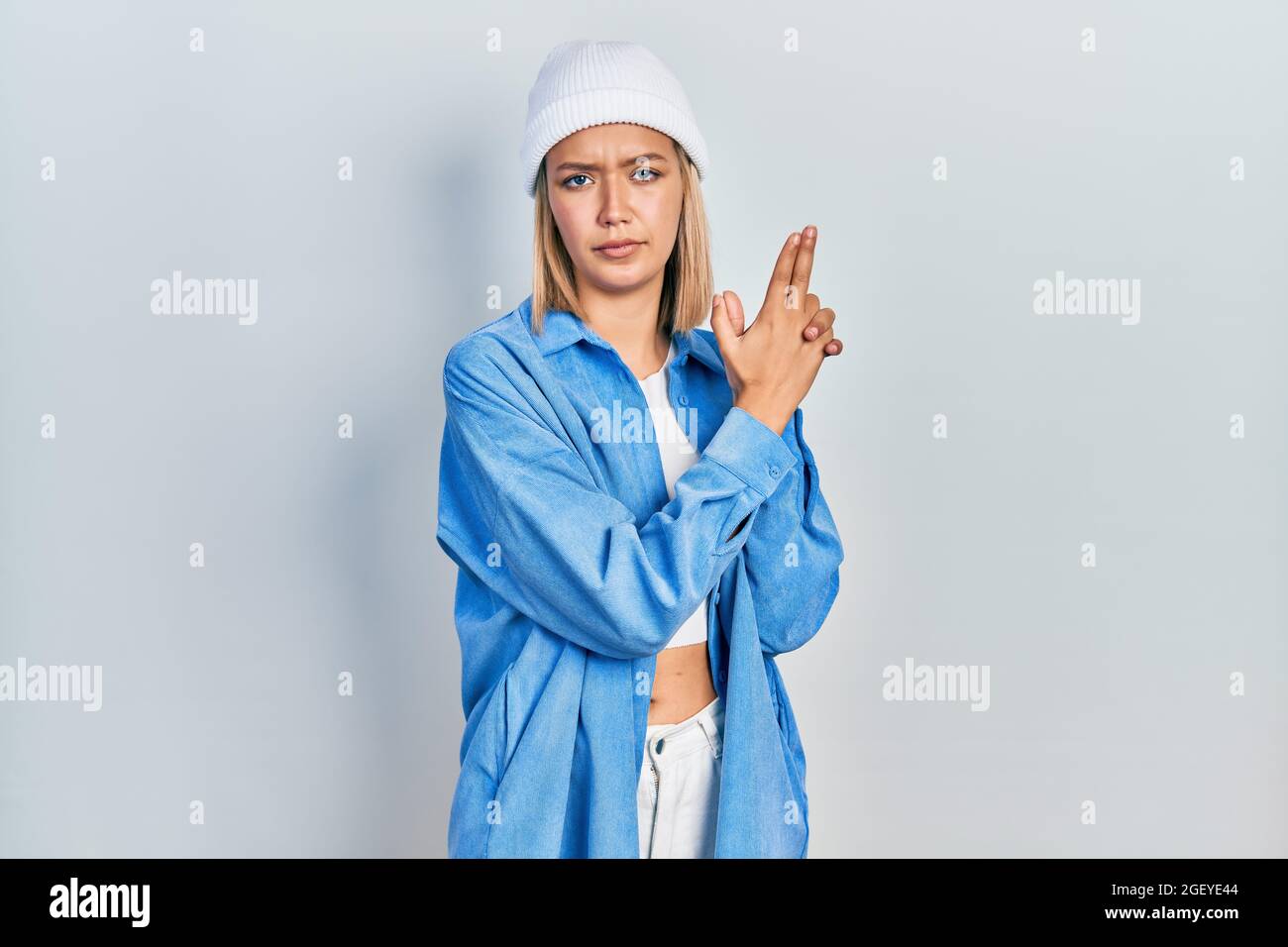 Beautiful blonde woman wearing wool hat holding symbolic gun with hand ...