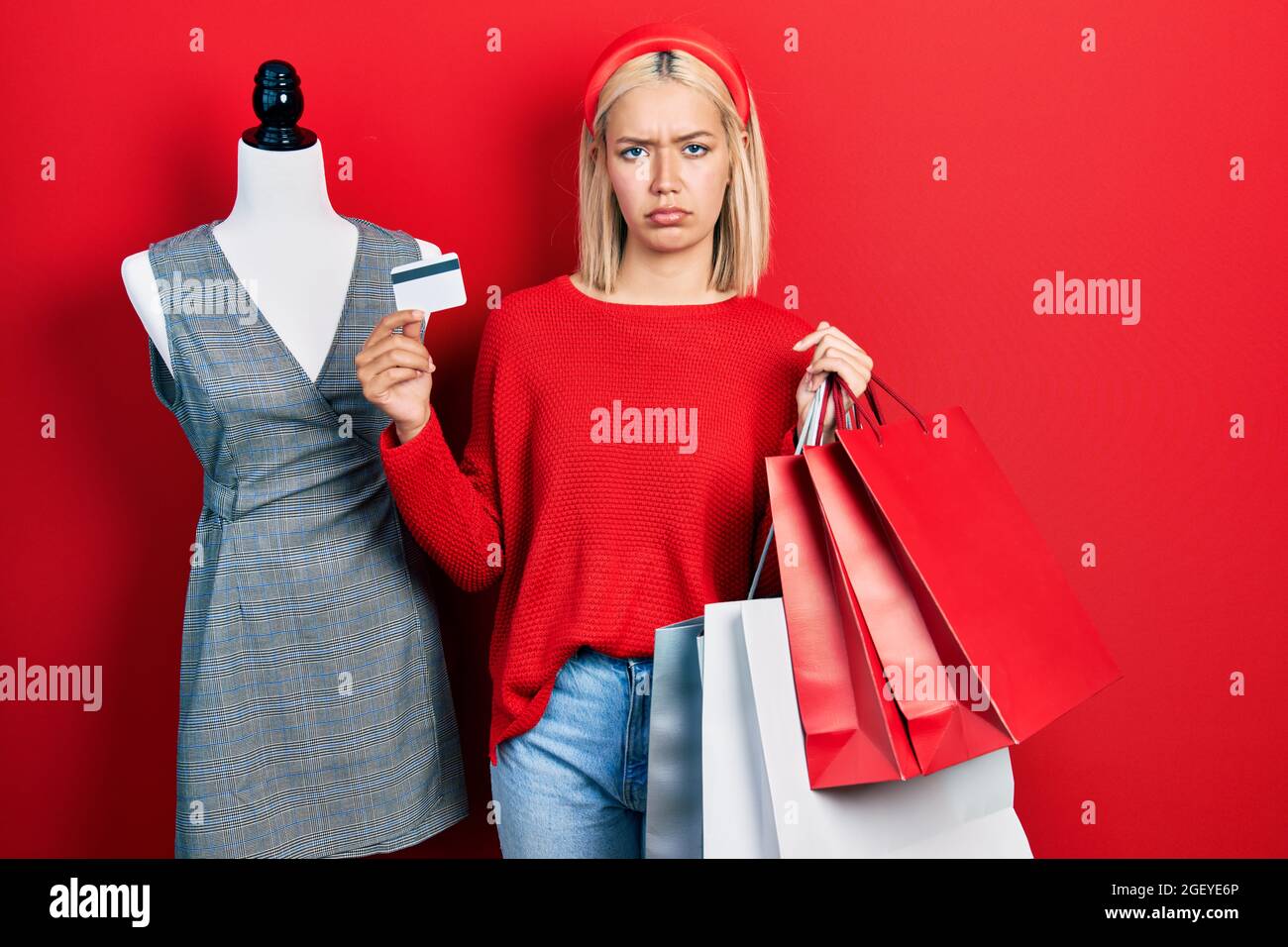 Beautiful blonde woman holding shopping bags and credit card depressed ...