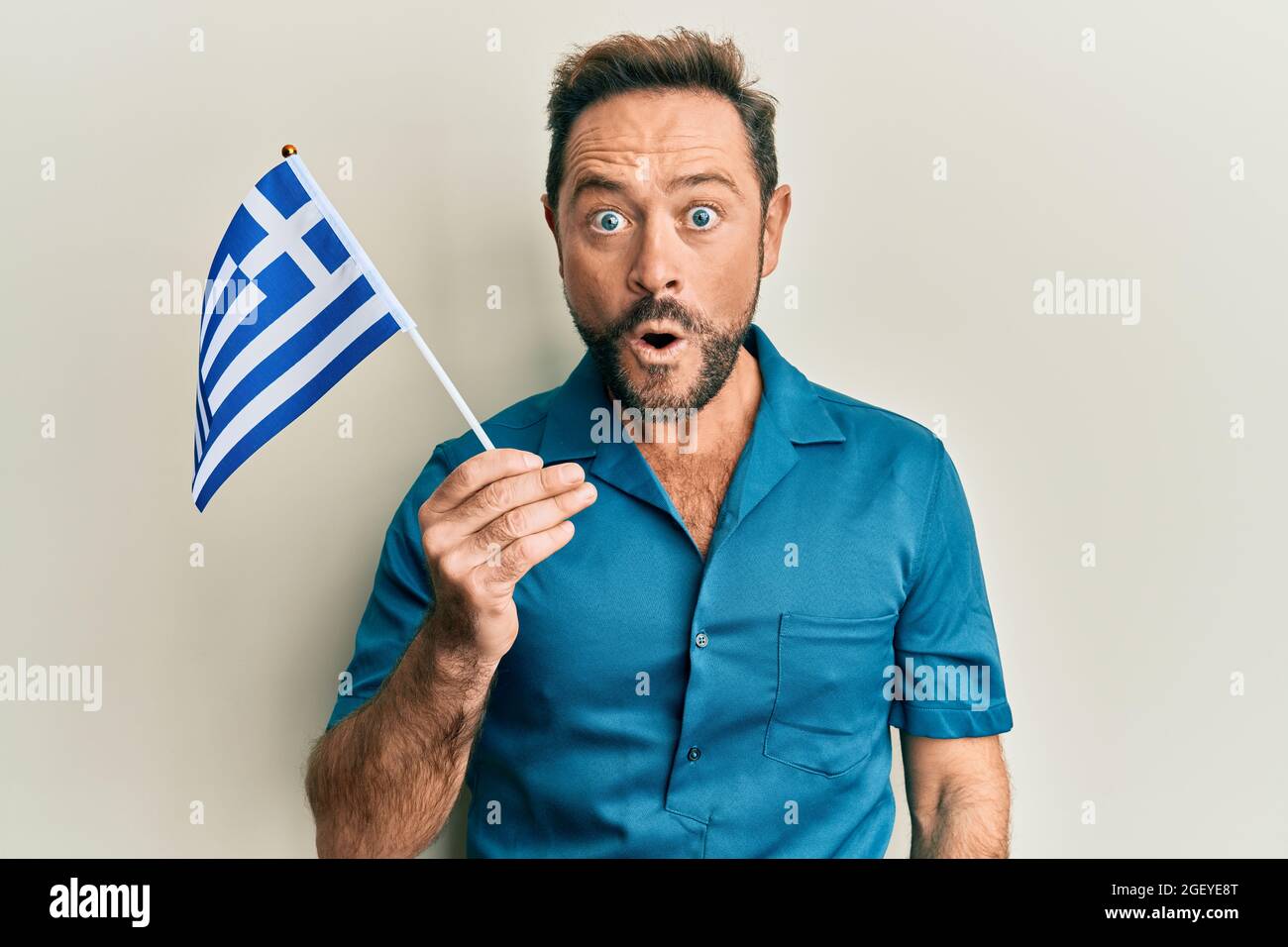 Middle age man holding greece flag scared and amazed with open mouth ...