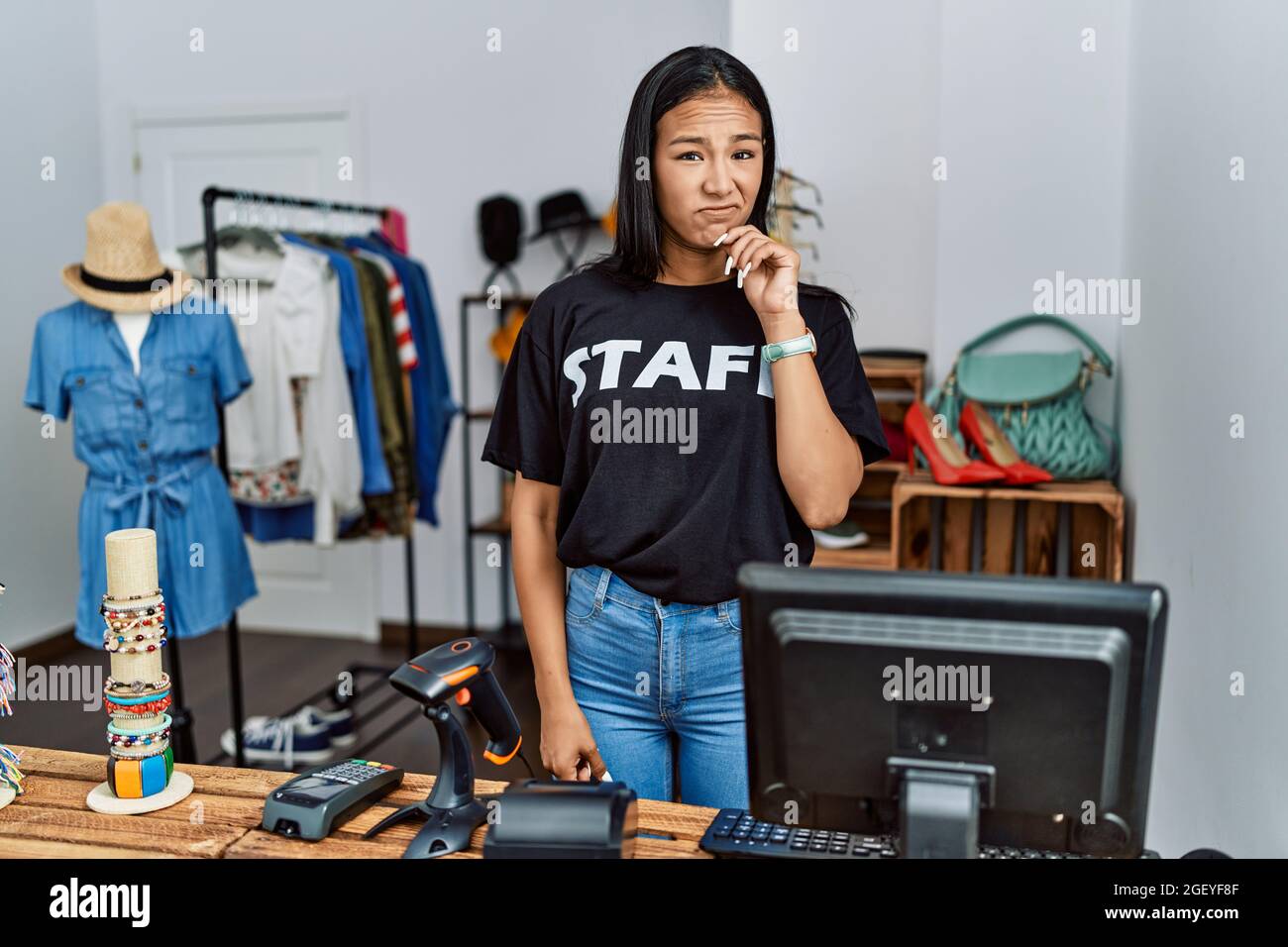 Young hispanic woman working as staff at retail boutique thinking ...