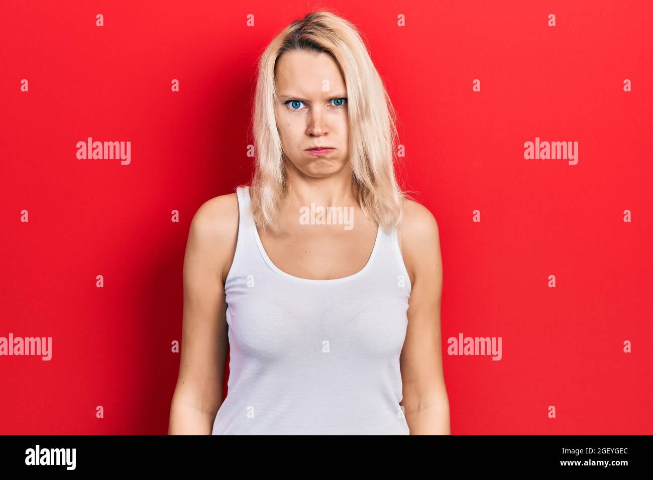 Beautiful caucasian blonde woman wearing casual white t shirt puffing ...