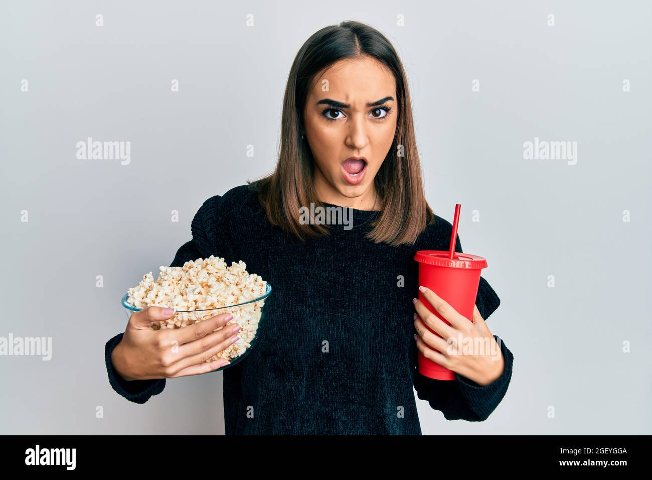 Young brunette girl eating popcorn and drinking soda in shock face ...