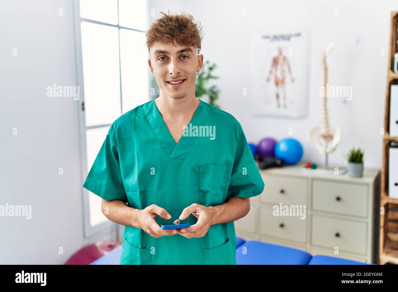 Young caucasian physio man using smartphone at medical clinic looking ...