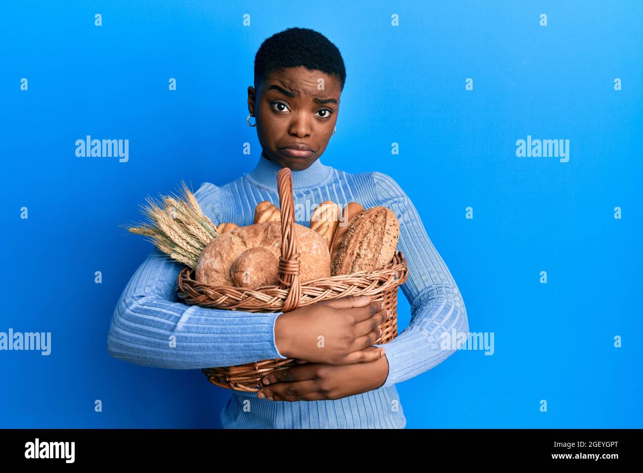 Young african american woman holding wicker basket with bread skeptic ...