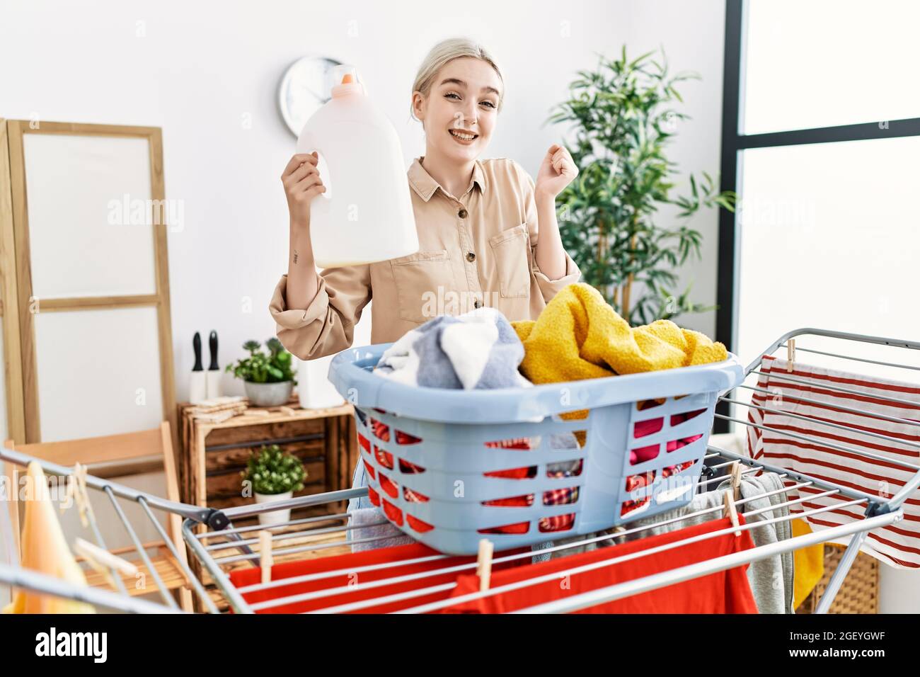 Young caucasian woman doing laundry holding detergent bottle screaming ...