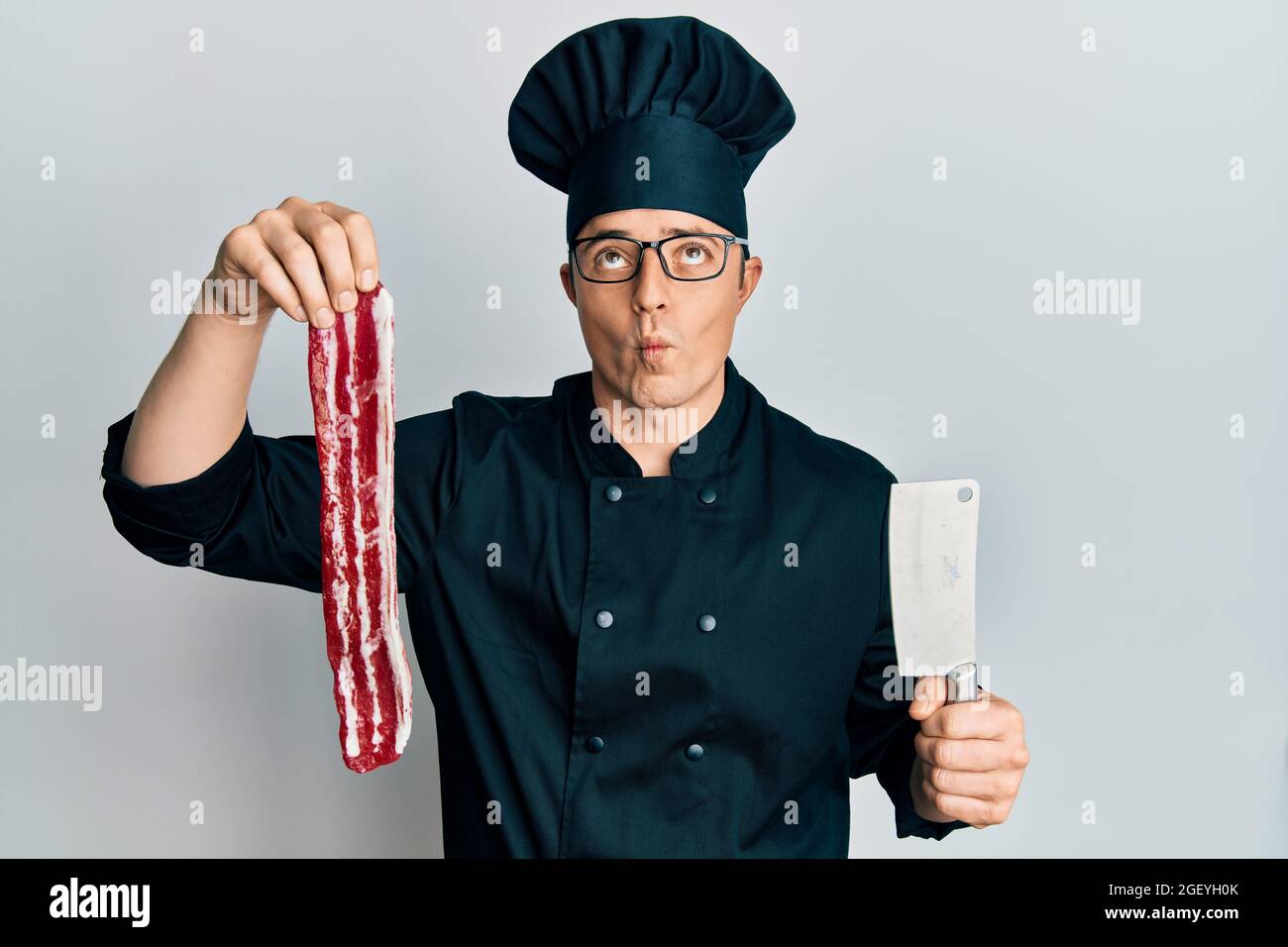Handsome young man wearing chef uniform holding bacon and knife making ...