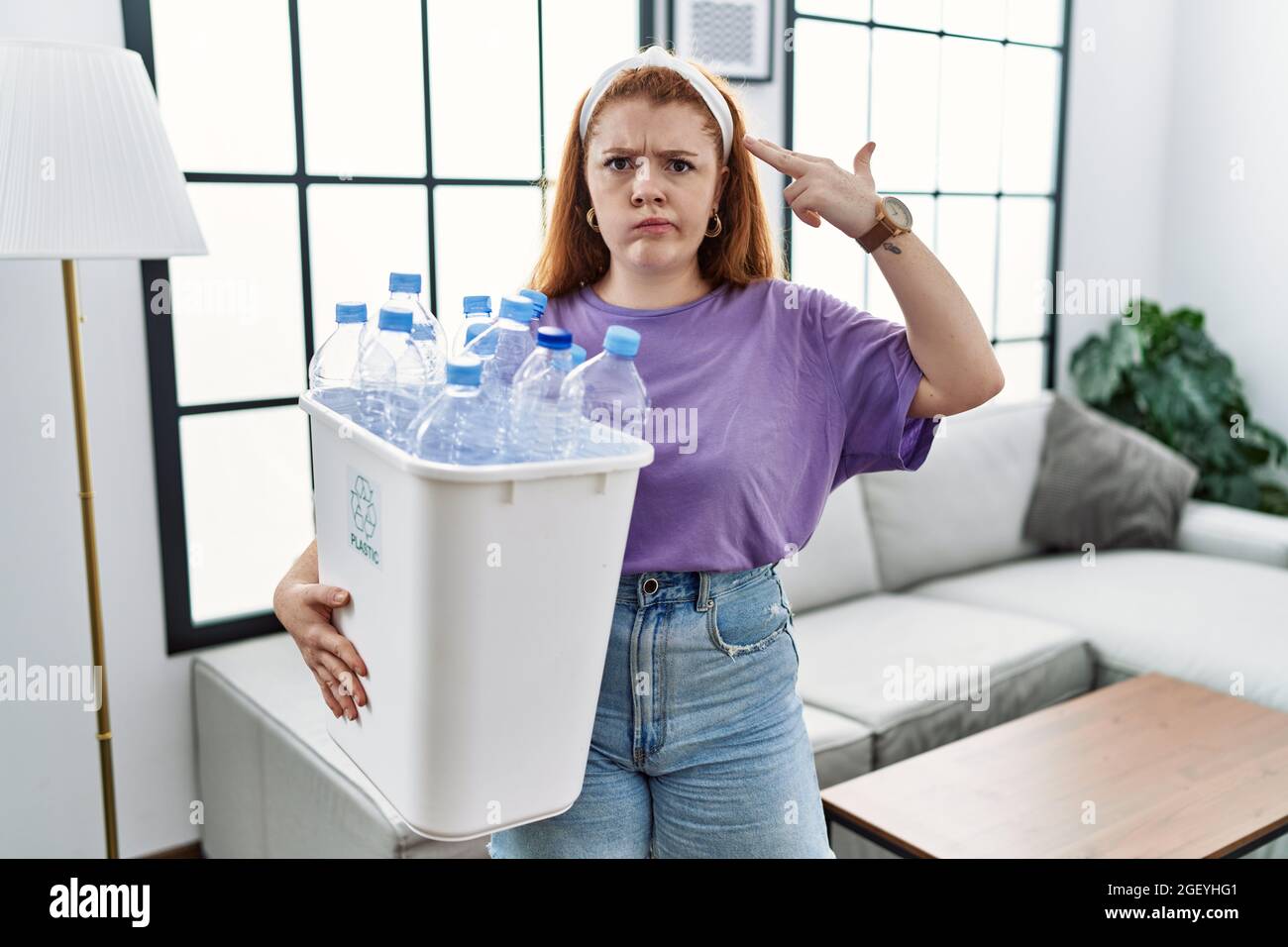 Young redhead woman holding recycling wastebasket with plastic bottles ...