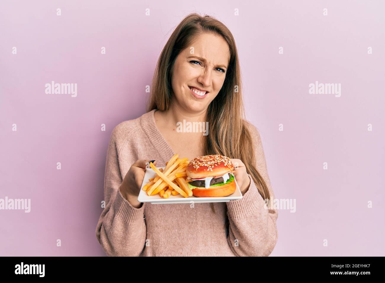Young blonde woman eating a tasty classic burger with fries clueless ...