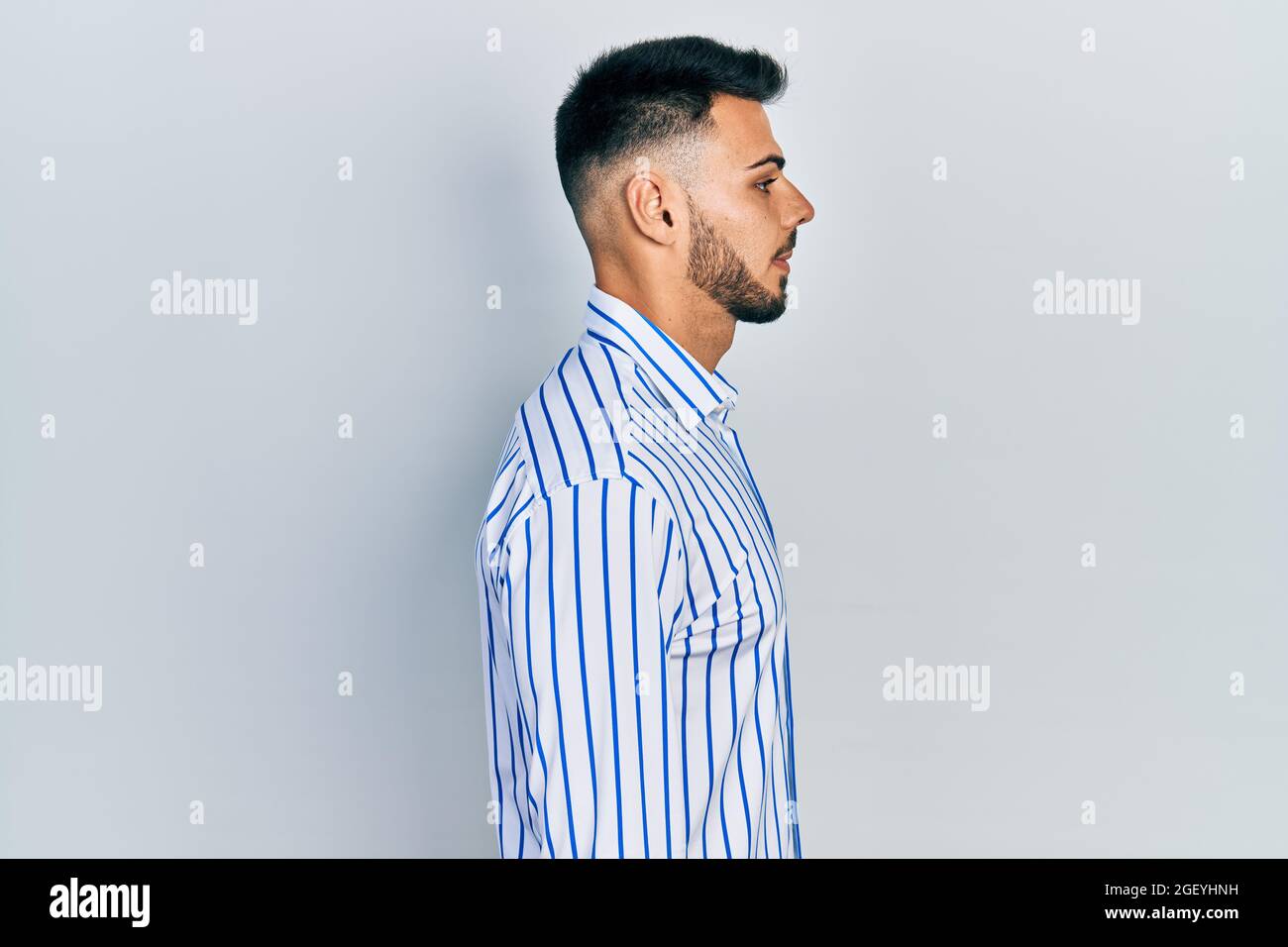 Young hispanic man with beard wearing casual striped shirt looking to ...