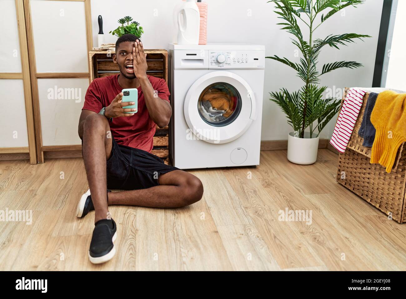 Young african american man using smartphone waiting for washing machine ...