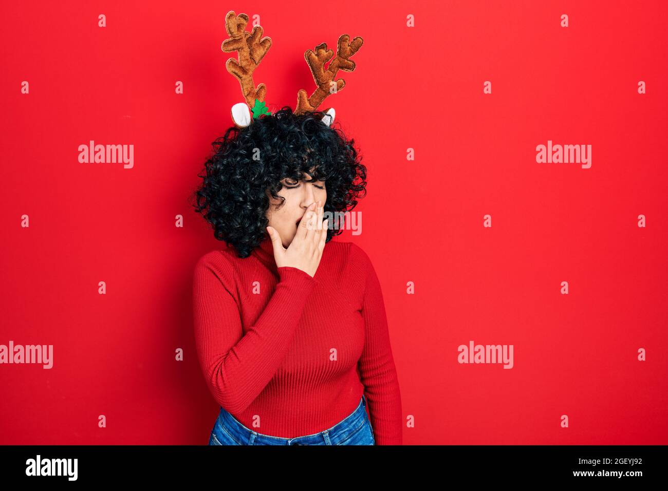 Young middle east woman wearing cute christmas reindeer horns bored ...