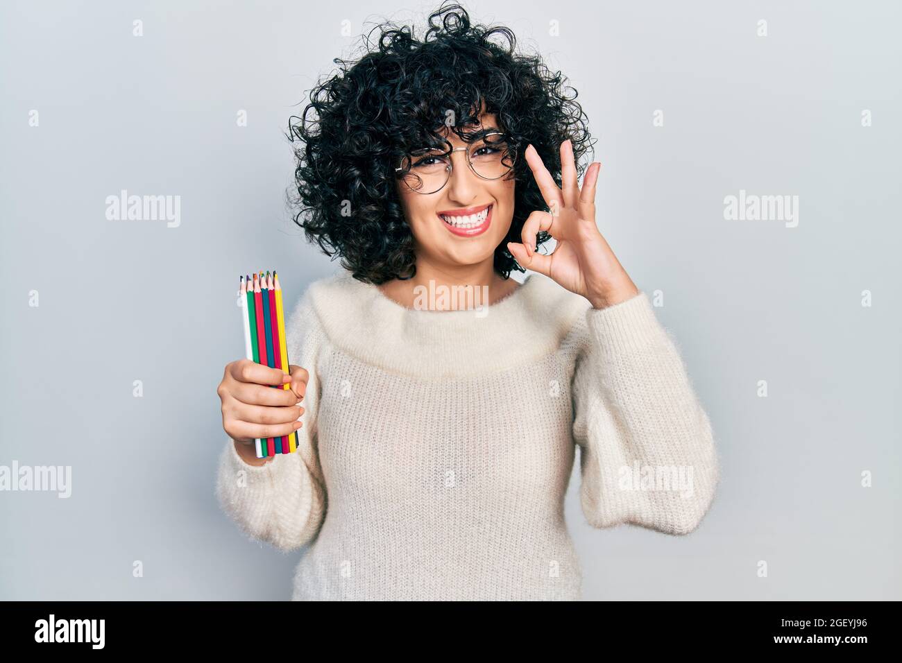 Young middle east woman holding colored pencils doing ok sign with ...